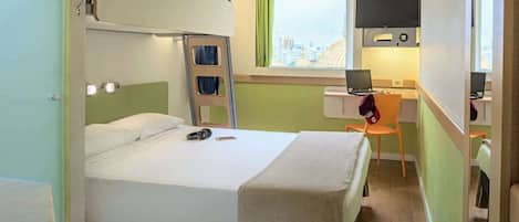 Quarto de hotel com beliche, uma secretária com um laptop, televisão e janela com vista para a cidade.