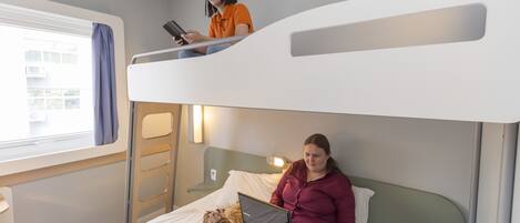 Quarto com beliche, um laptop na cama inferior e uma pessoa sentada na cama superior.