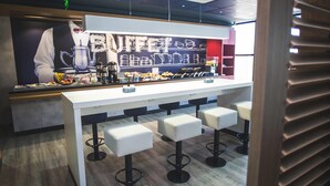 Uma área de bar moderna com um balcão longo, vários bancos e uma variedade de alimentos e bebidas dispostos.