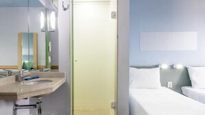 Quarto de hotel com banheiro, uma cama e uma mesa de cabeceira.