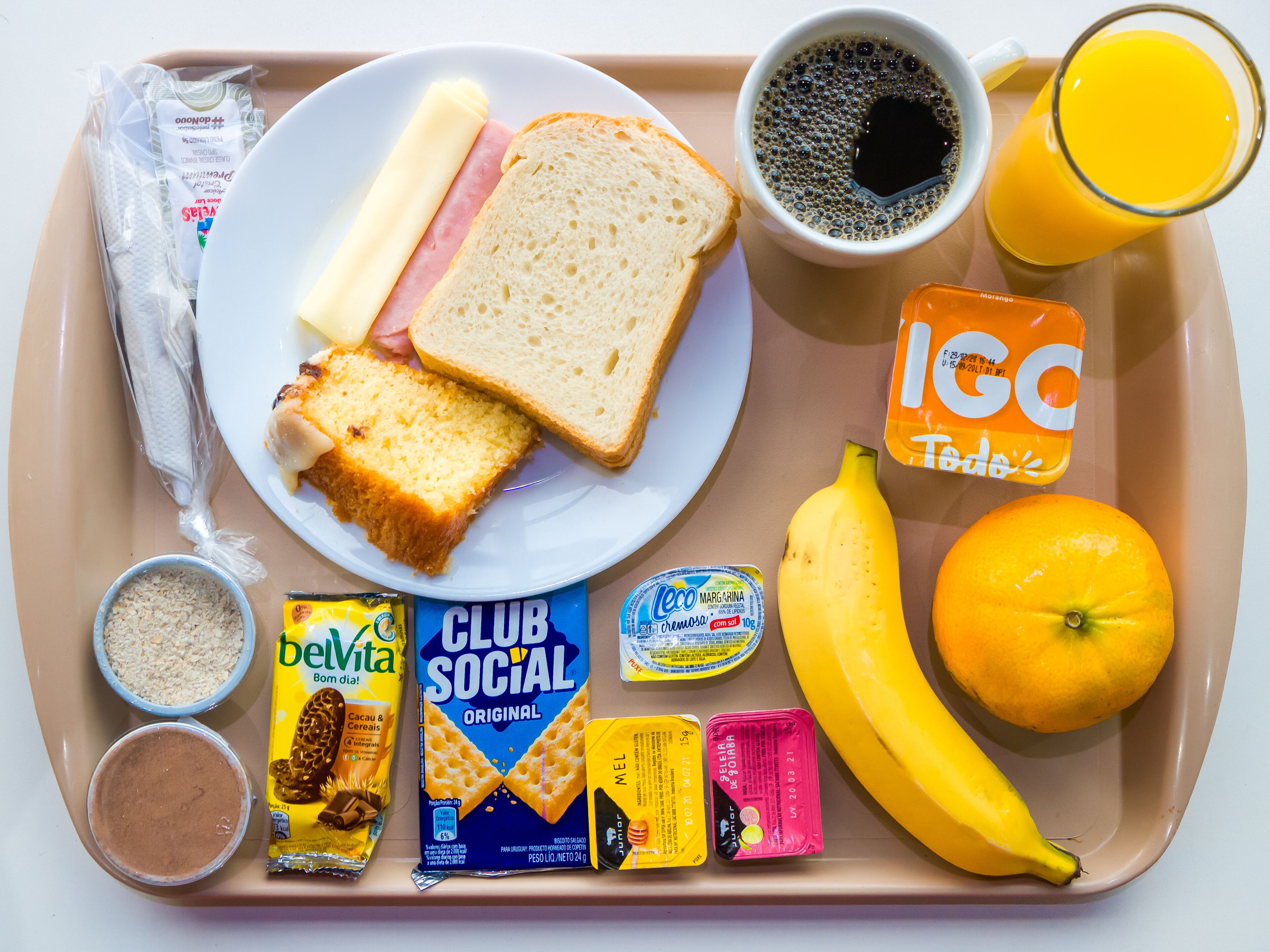 Uma bandeja com itens de café da manhã, incluindo torradas, geleia, café, suco de laranja, uma banana, uma laranja, cereal, uma barra de chocolate e um sachê de chá.