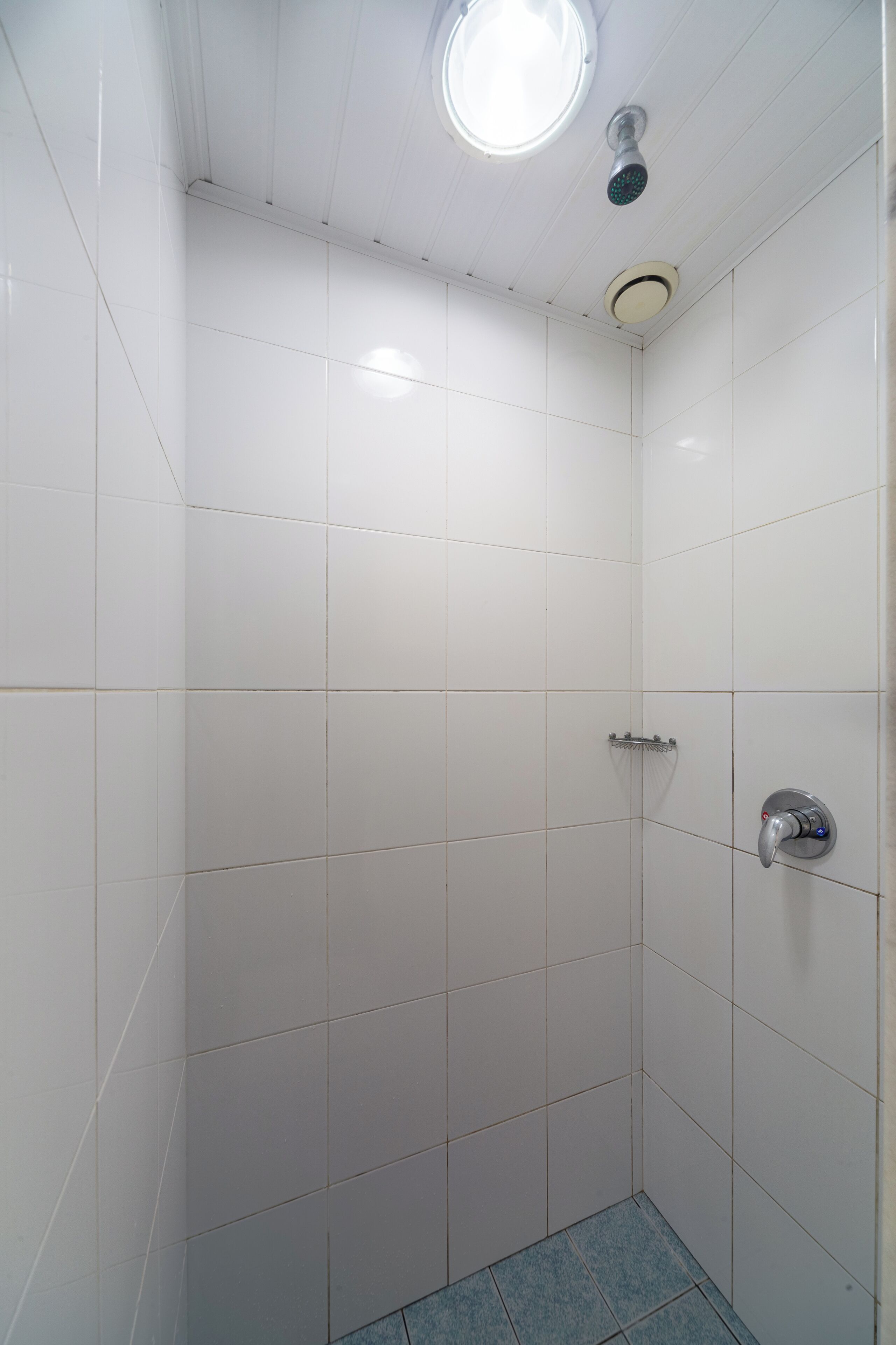 Um pequeno banheiro revestido com azulejos, com uma lâmpada no teto e um chuveiro.
