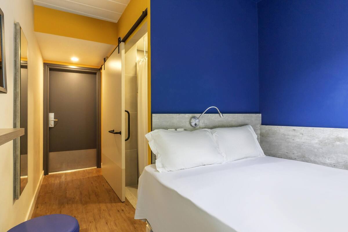 Quarto com cama, parede azul e chão de madeira.