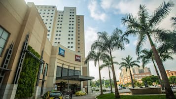 Um hotel com fachada moderna, entrada coberta e palmeiras em primeiro plano.