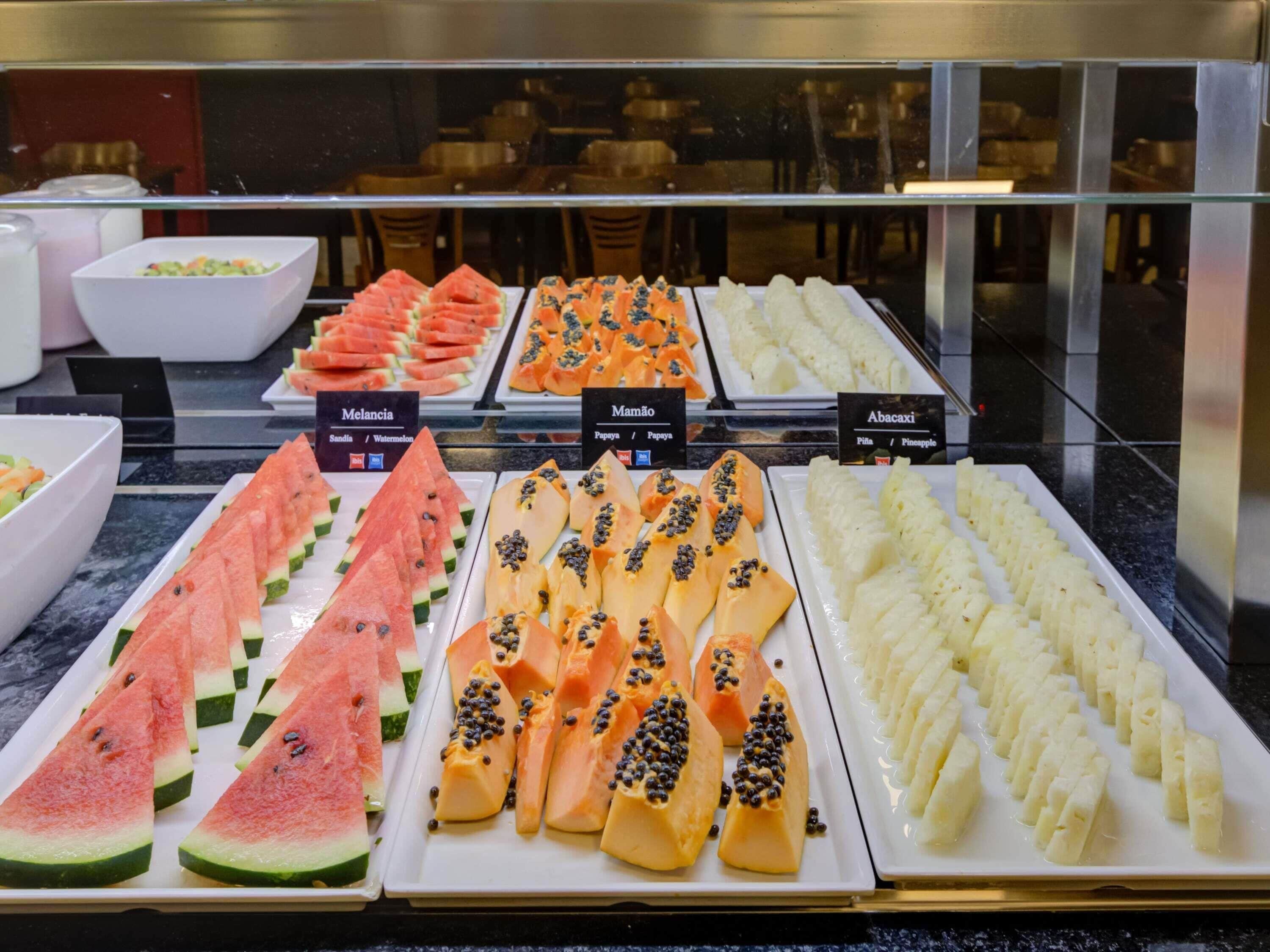Buffet com diversas frutas e legumes, incluindo melancia, mamão e abacaxi.
