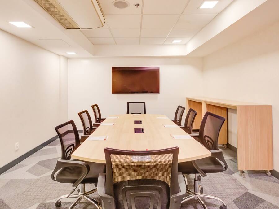 Uma sala de conferências com uma mesa comprida, cadeiras, uma tela de projetor e um pequeno armário.