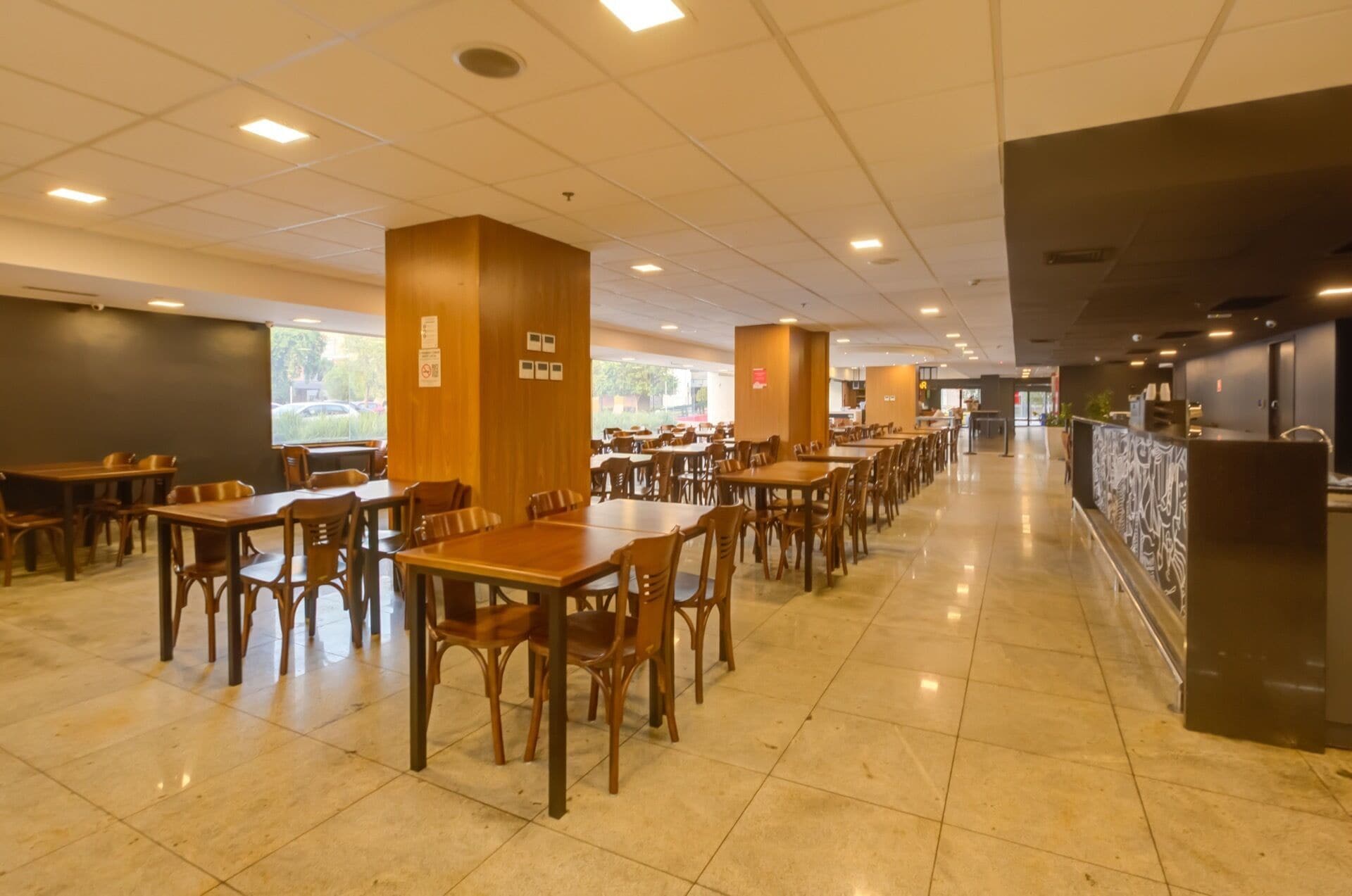 Um restaurante espaçoso com mesas e cadeiras de madeira, piso de azulejos e um balcão com cardápio.