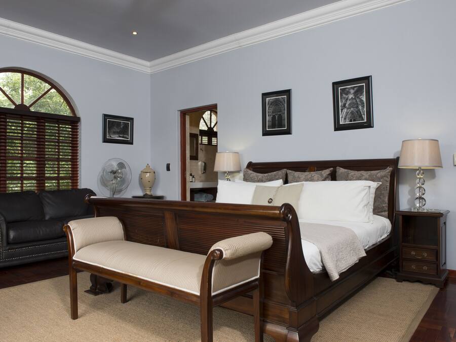 Quarto com cama de madeira, um banco, sofá de couro preto e um ventilador.