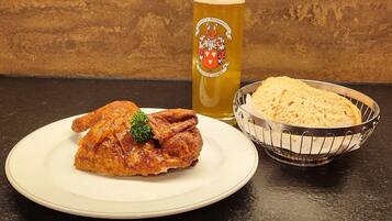 Um prato com frango frito, uma garrafa de cerveja e uma tigela de pão sobre uma mesa.