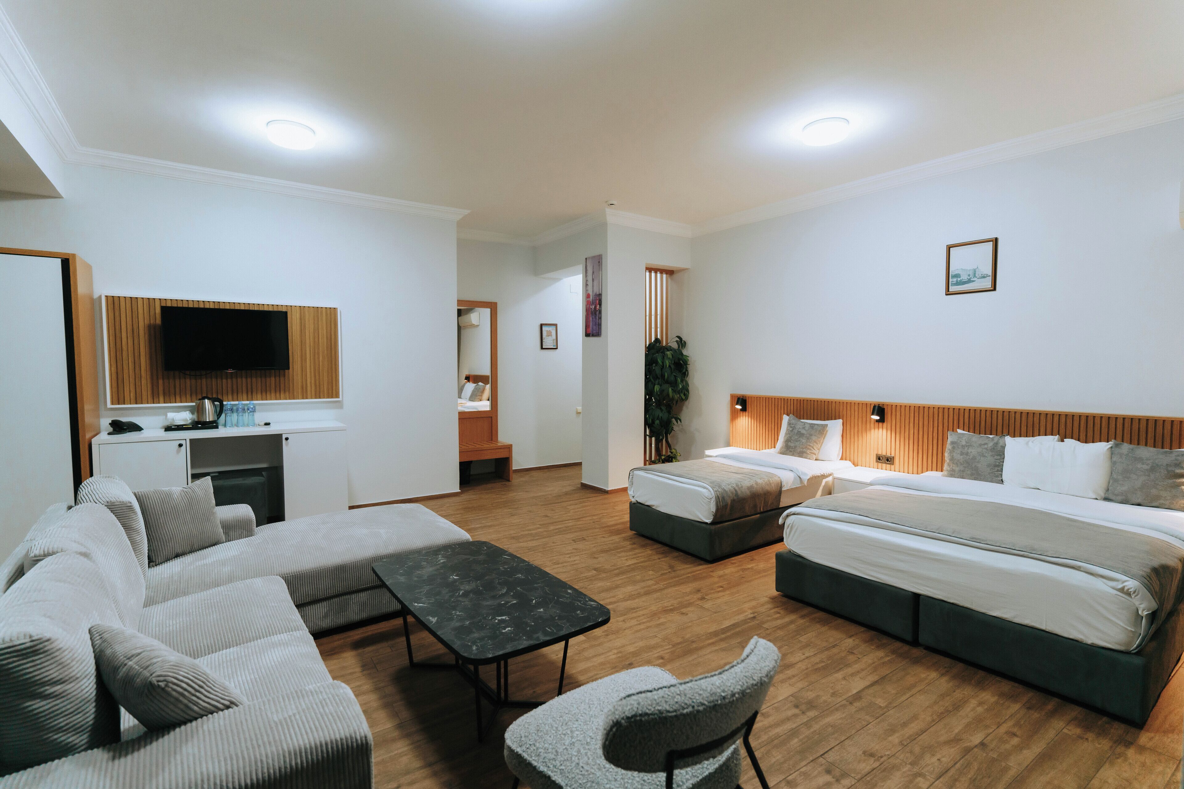 Quarto de hotel moderno com sofá, duas camas de solteiro, uma escrivaninha pequena e televisão.