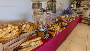 Buffet com diversos pães, frutas e um arranjo decorativo de plantas.