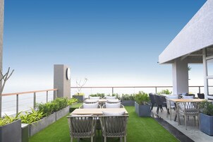 Terraço no telhado com mesas ao ar livre, um relógio e vista para o mar.