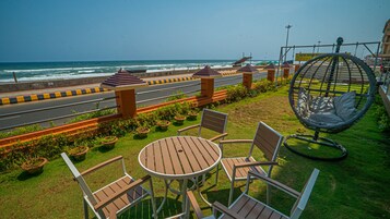 Um alpendre à beira-mar com mesa e cadeiras redondas, uma cadeira suspensa e vista para o oceano.