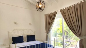 Quarto com cama, mesa de cabeceira, janela com cortinas e luminária pendente.