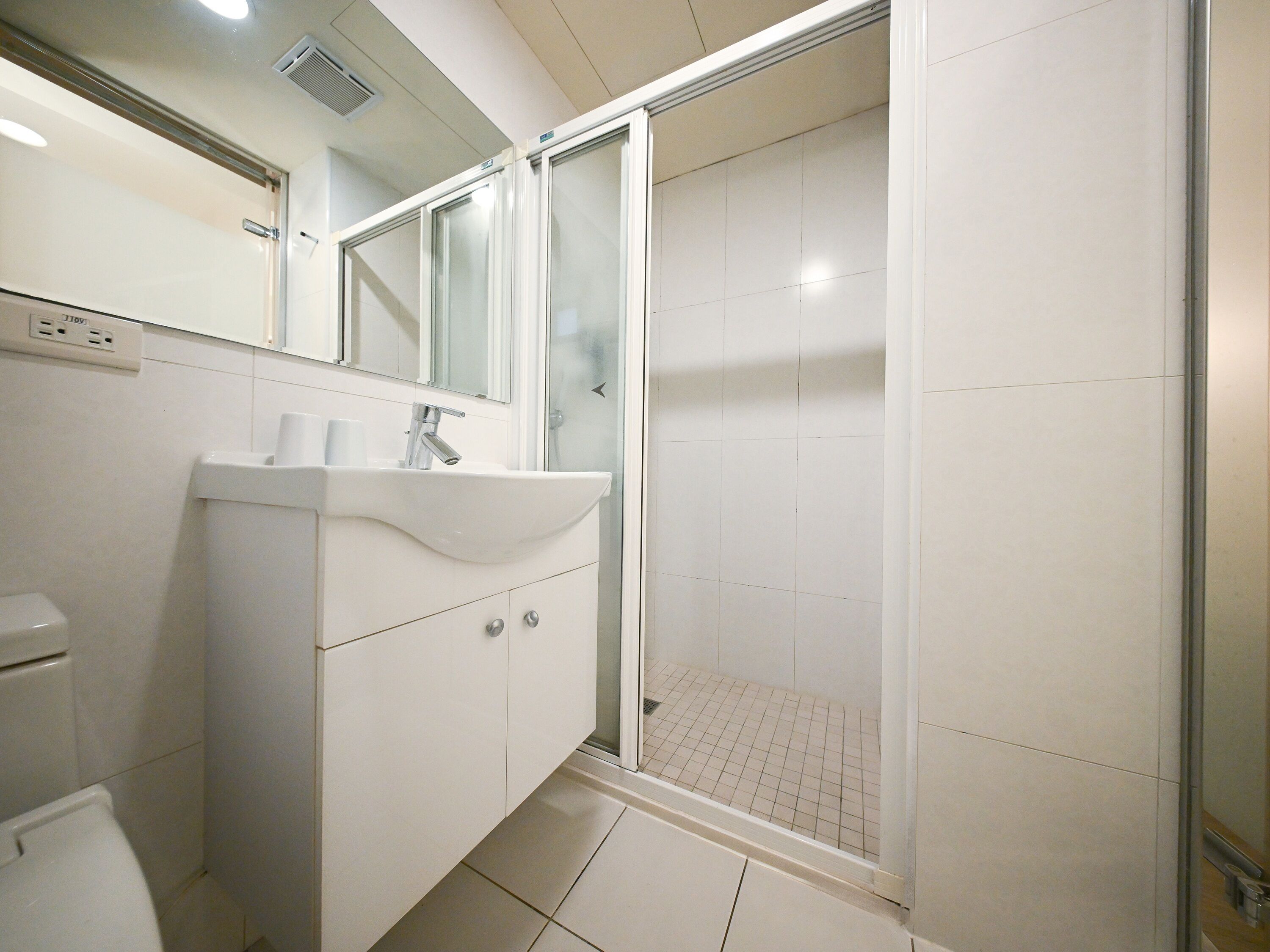 Casa de banho com lavatório branco, espelho e cabine de duche.