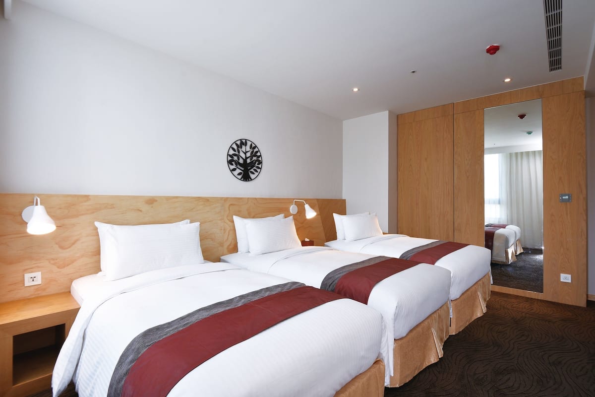 Quarto de hotel com duas camas, cabeceiras de madeira, roupa de cama branca e um espelho em uma das paredes.