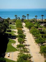 Uma trilha arborizada com bancos, que leva a uma praia.
