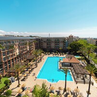 Um resort com uma piscina grande, espreguiçadeiras, guarda-sóis e vista para o mar.