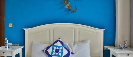 Quarto com cabeceira branca, almofada estampada em azul e branco, e decoração de pássaros dourados na parede.