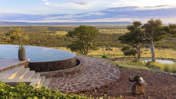 Uma piscina de pedra circular com degraus que a rodeiam, inserida em paisagem natural com árvores e vista para colinas ao longe.
