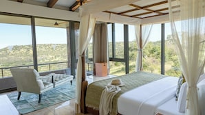 Quarto com cama grande, uma cadeira e vista para o exterior.