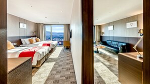 Quarto de hotel com duas camas, um sofá, uma escrivaninha e vista para a cidade.
