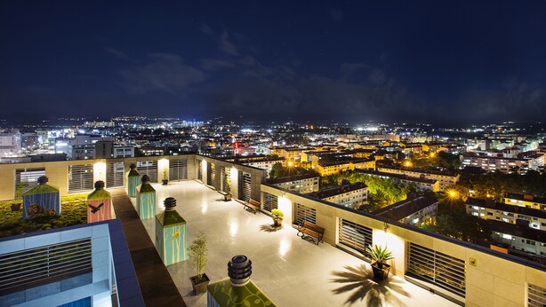 Terraço no telhado com vista para a cidade à noite.