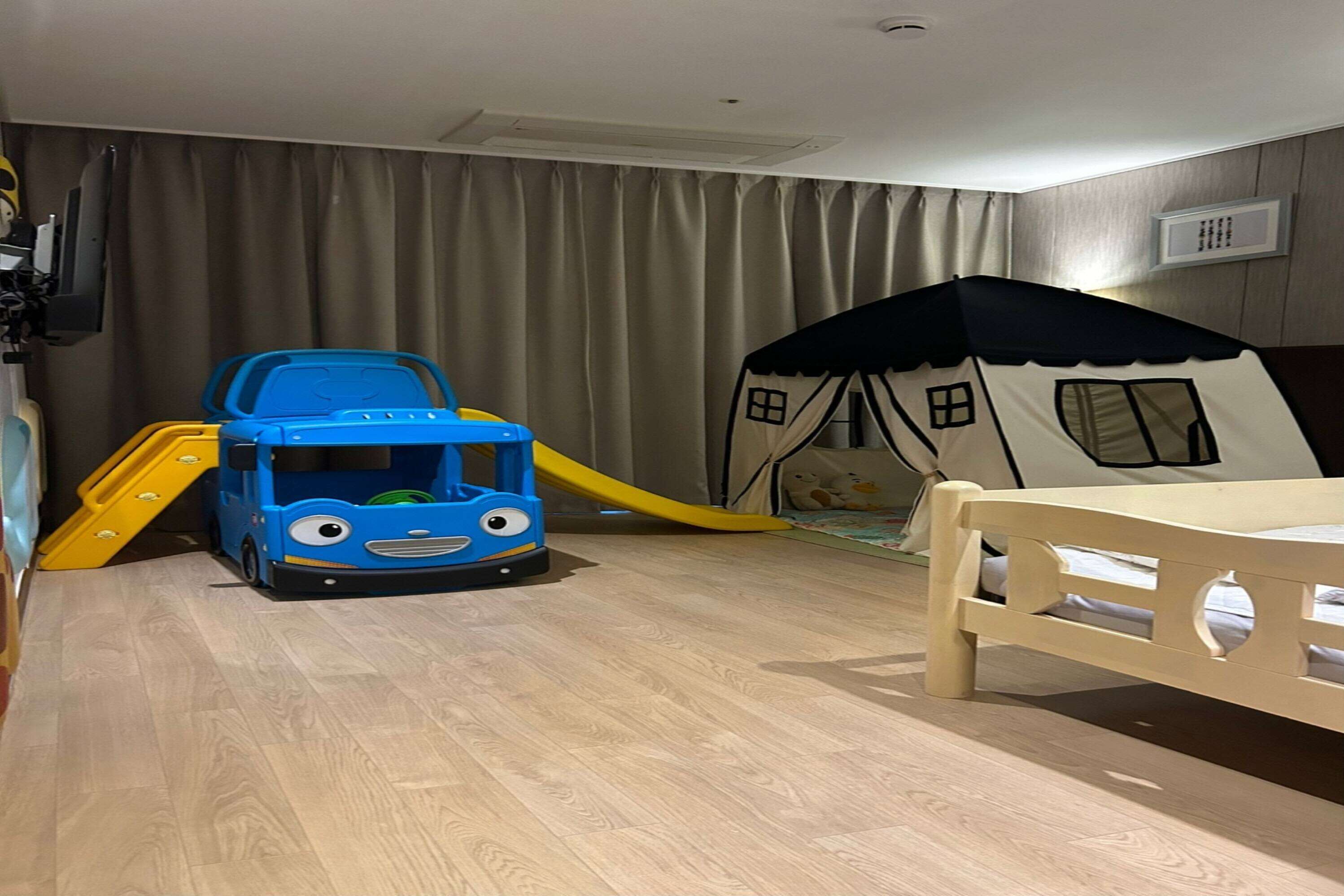 Quarto com área de recreação, incluindo um carrinho de brinquedo azul e uma tenda.