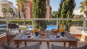 Mesa de varanda com itens de café da manhã, com vista para uma piscina e edifícios residenciais.
