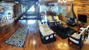 Uma sala de estar ampla com lareira, assentos e escada que leva a um andar superior.