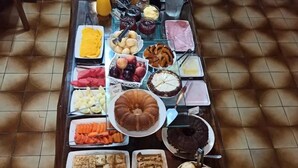 Uma mesa de buffet com diversos alimentos, incluindo frutas, doces e sobremesas.