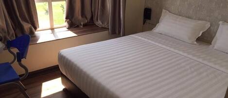 Quarto de hotel com uma cama grande, uma cadeira e uma janela com cortinas.