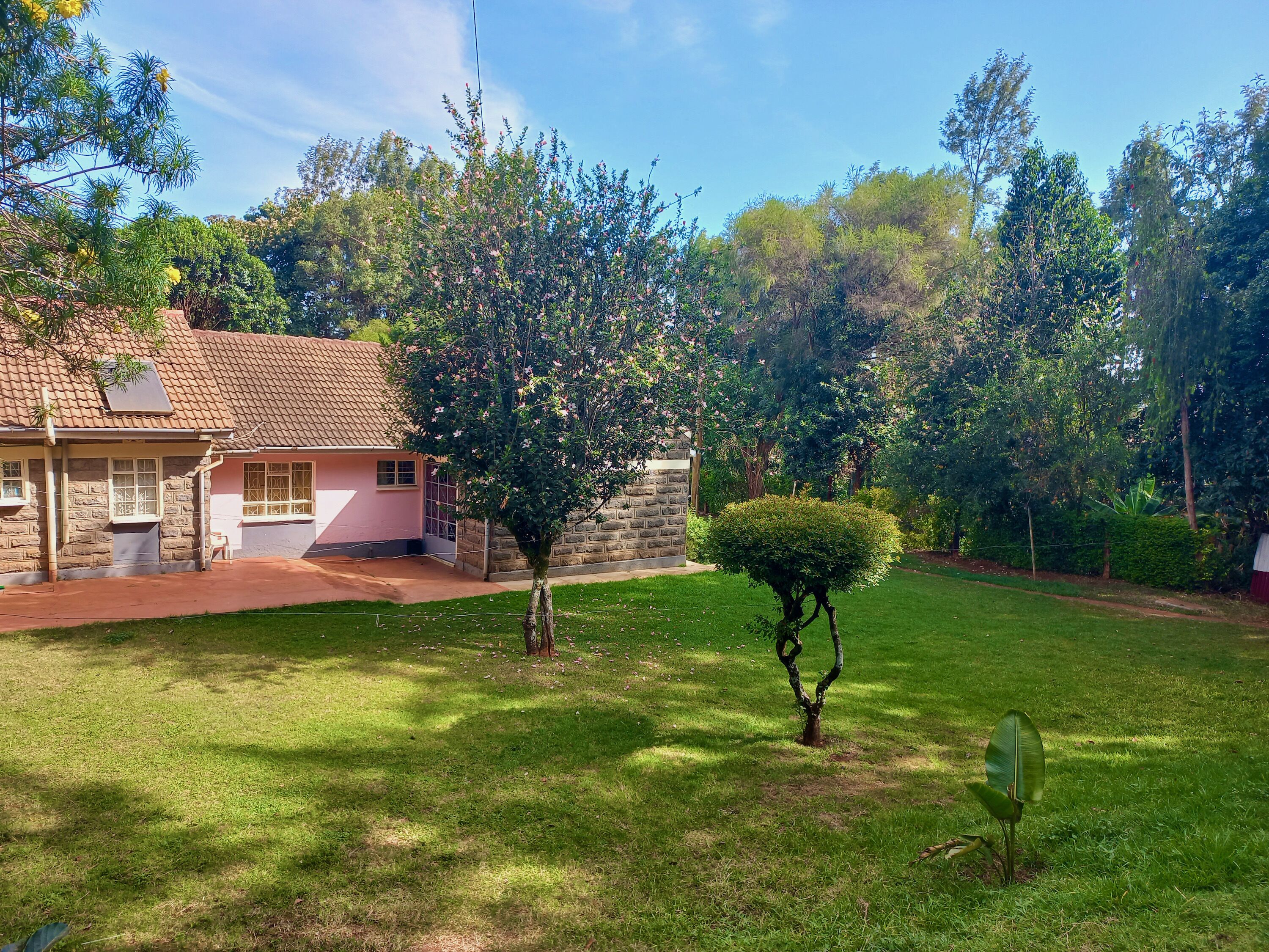 Uma casa com fachada de pedra e telhado de telhas, cercada por um gramado bem cuidado e diversas árvores.