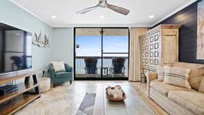 Uma sala de estar com televisão, ventilador de teto, sofá e vista para o oceano através de grandes portas de correr.