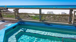 Uma piscina com água azul cristalina, um deck de madeira e vista para a praia e oceano.