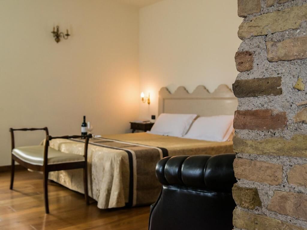 Um quarto com cama, uma cadeira, uma mesa com uma garrafa e um paredão de tijolos.
