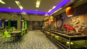 Um restaurante moderno com piso estampado, cadeiras verdes e um balcão exibindo alimentos.