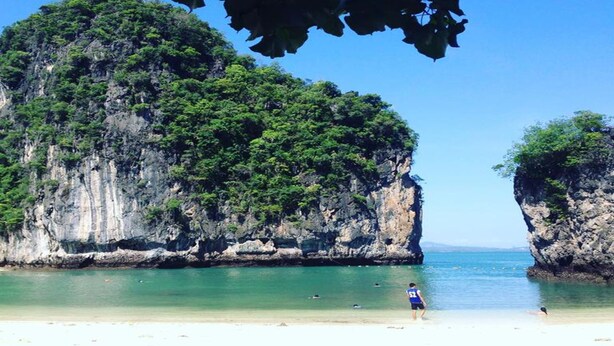 Uma praia com águas turquesa cristalinas, falésias rochosas e vegetação exuberante.