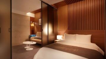 Quarto de hotel com cama, cadeira, mesinha e parede de painéis de madeira.