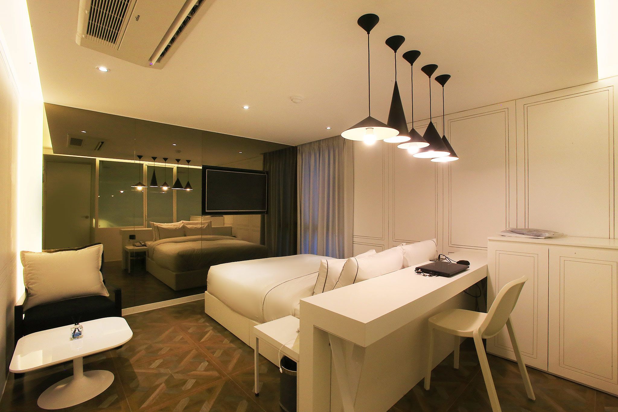 Quarto de hotel moderno com cama, escrivaninha, cadeira e televisão.