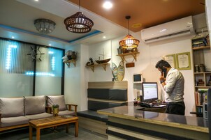 Um hall de hotel moderno com uma mesa de recepção, um sofá, uma mesa de centro e objetos decorativos como um modelo de navio e pranchas de surf.