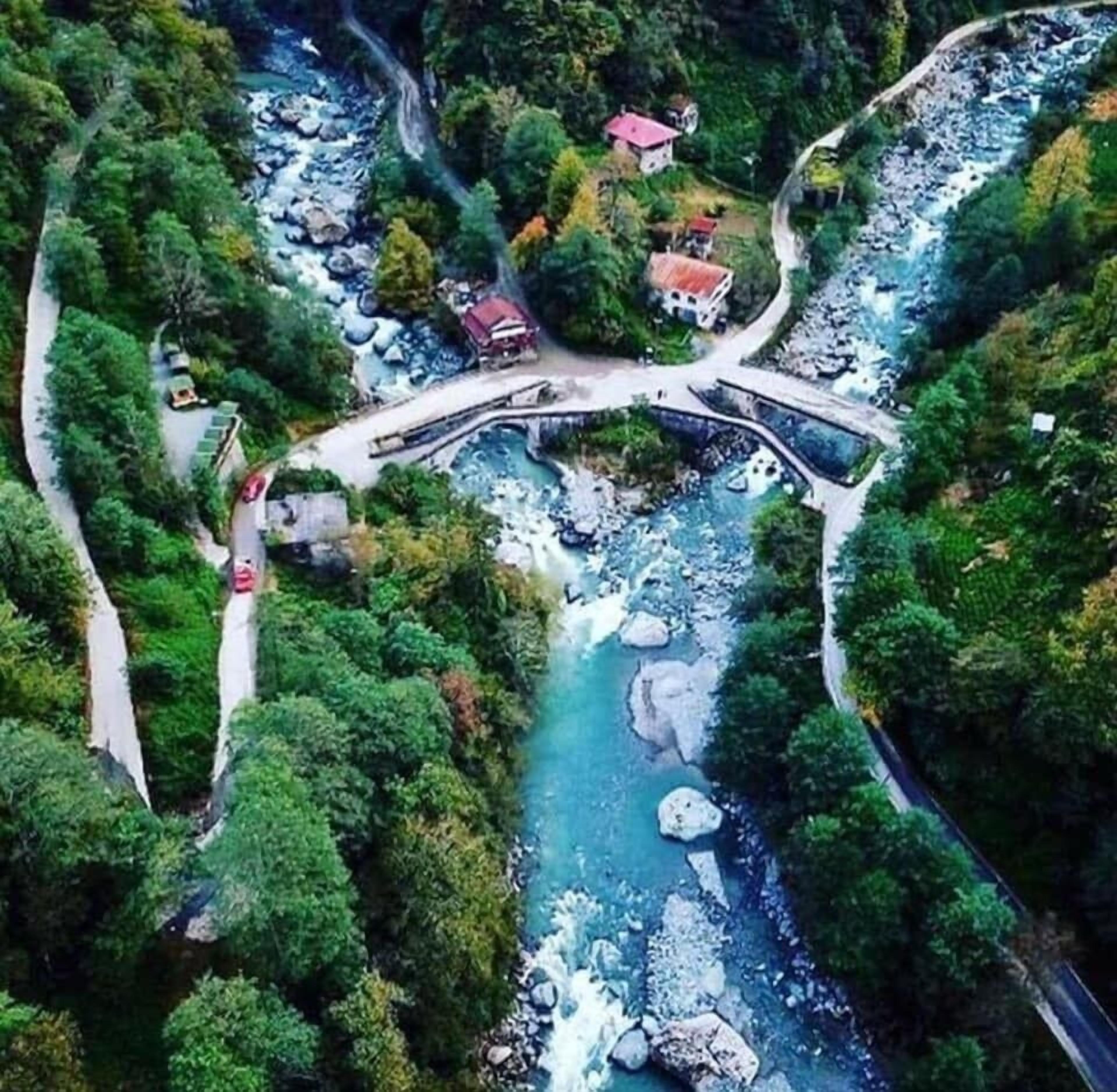 Um rio serpenteando por uma área arborizada, com uma ponte e alguns edifícios.