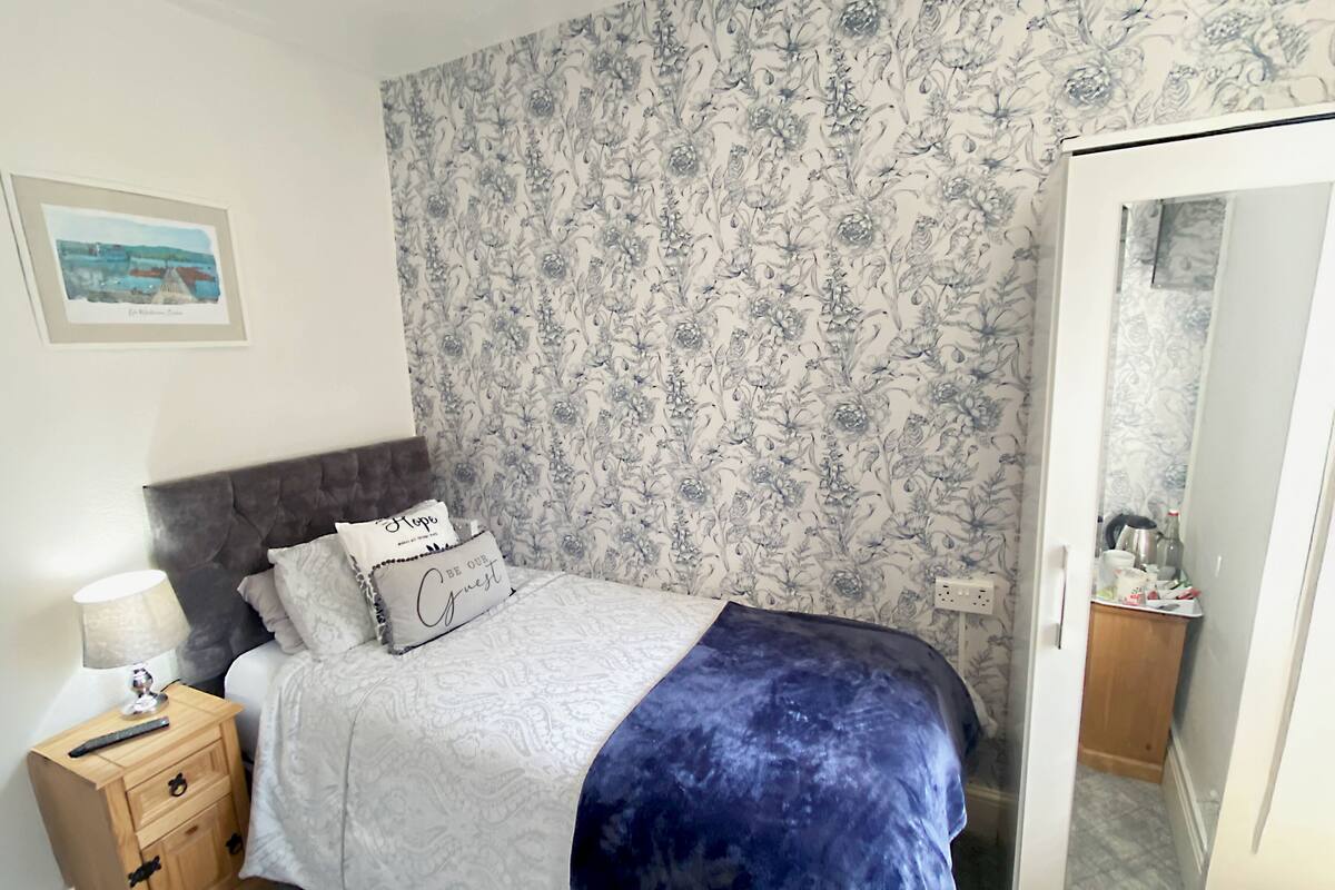 Quarto com cama, mesa de cabeceira, guarda-roupa e papel de parede floral.