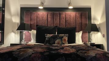 Quarto com cama grande, duas luminárias de cabeceira, cabeceira com painéis verticais e colcha floral.