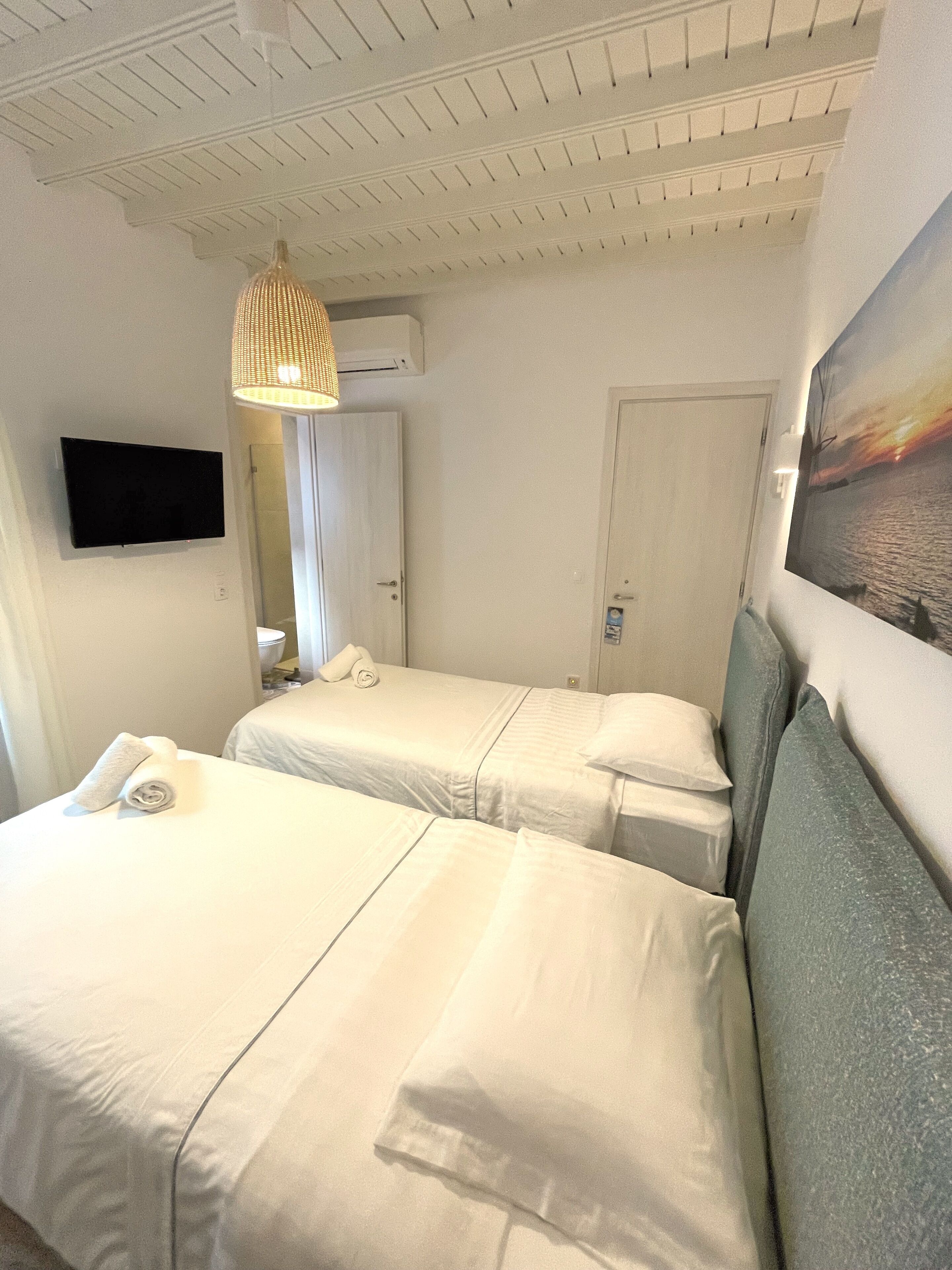 Quarto de hotel com duas camas, uma televisão, um quadro e um ventilador de teto.