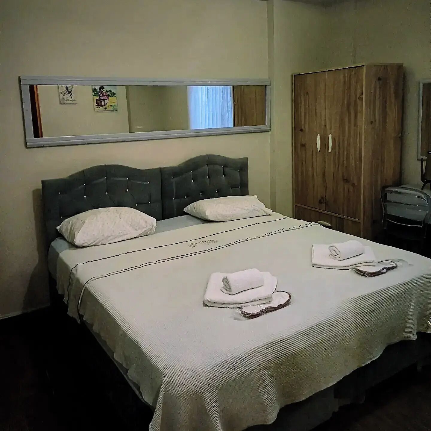 Uma cama bem arrumada com almofadas e toalhas, um guarda-roupa de madeira e um espelho na parede.