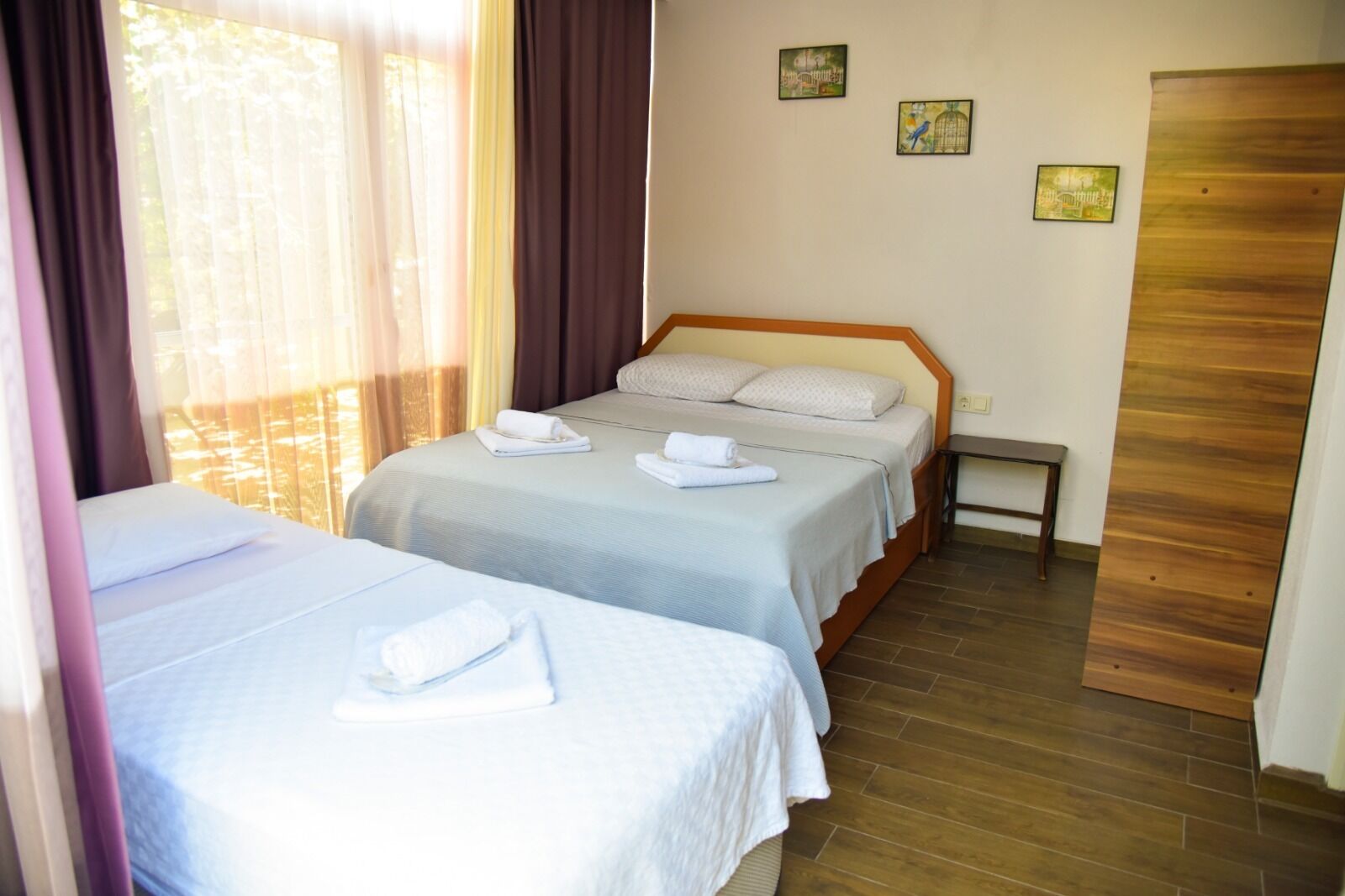 Quarto de hotel com duas camas, piso de madeira e uma pequena mesa de cabeceira.