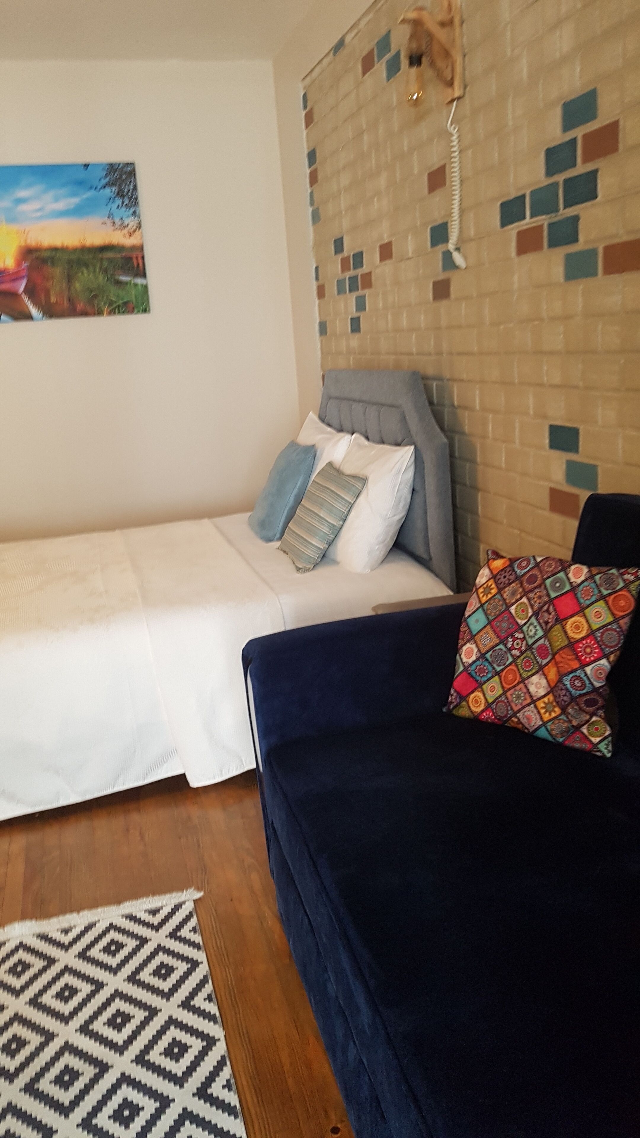 Quarto com cama, um sofá azul, tapete estampado e parede com desenho em mosaico.