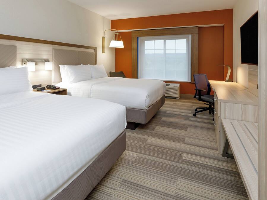 Quarto de hotel com duas camas, uma escrivaninha, uma cadeira, uma televisão e uma janela.