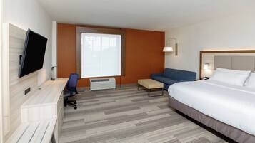 Quarto de hotel com cama, escrivaninha, televisão de tela plana, cadeira azul, mesinha e janela.